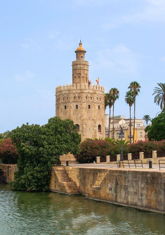 The Torre del Oro golden tower standing beside the Guadalquivir River in Seville with palm trees