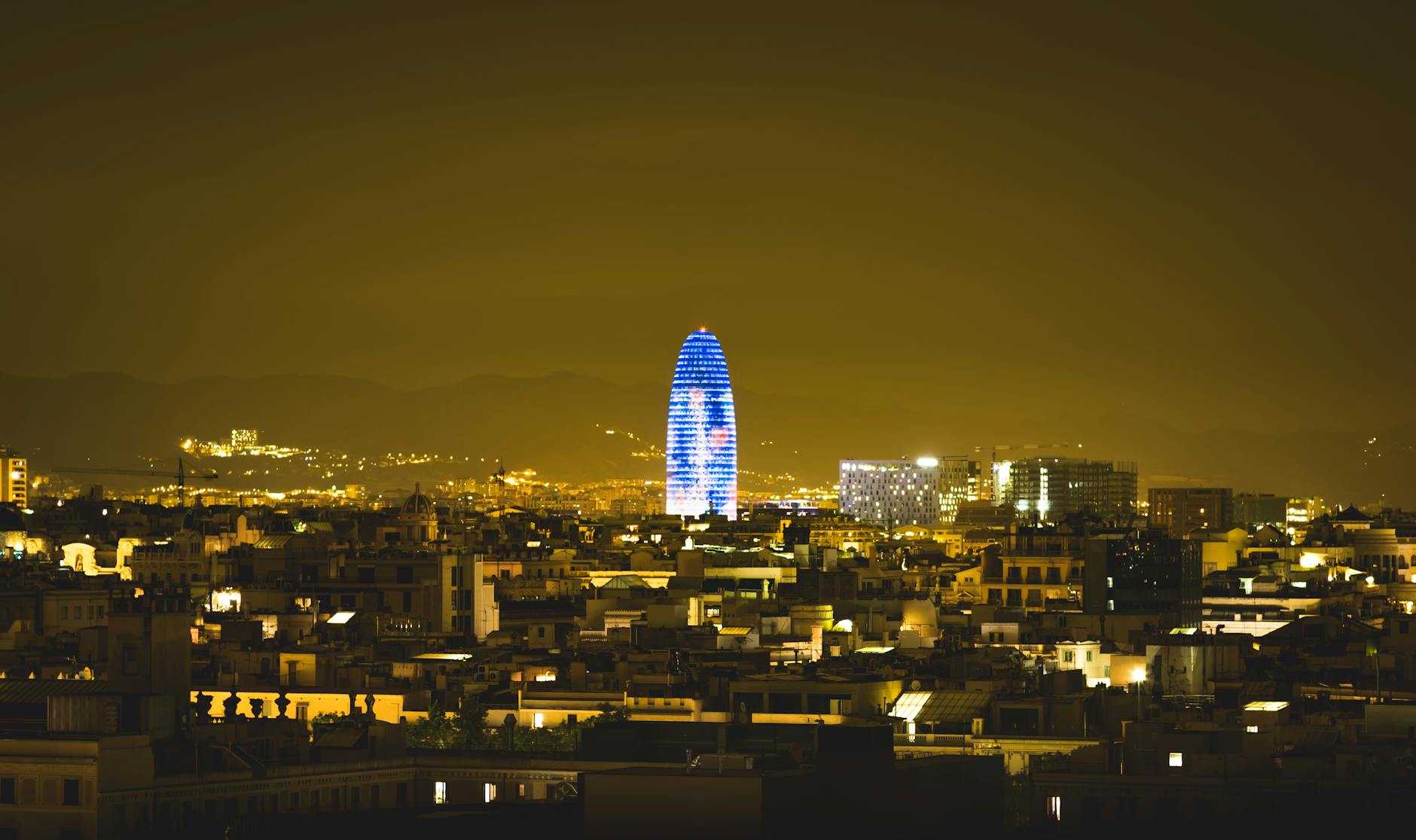 Torre Glories illuminated at night against the Barcelona cityscape