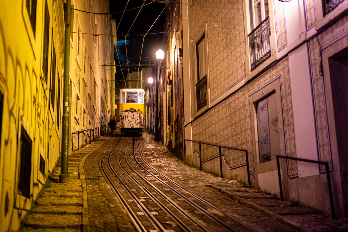 Tram navigating steep Lisbon tracks at night under warm street lighting