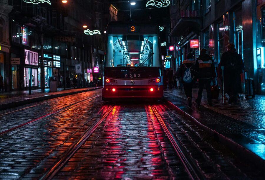 Prague tram running down a wet cobblestone street reflecting city lights on a rainy evening