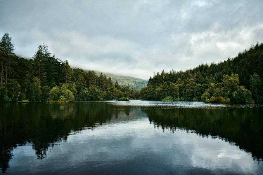 A small boat sailing across the calm dark waters of Loch Ness with the green hillside of the Scottish Highlands in the background