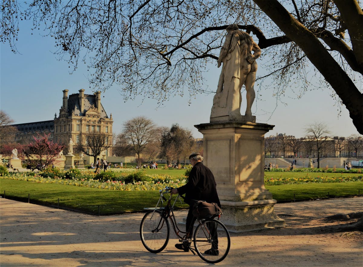 Cyclist passing a statue in the Tuileries Garden with the Louvre Palace in the background