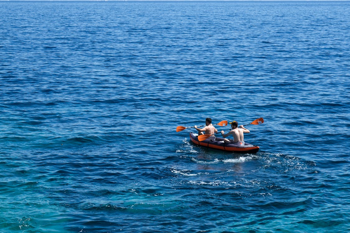 Two men kayaking on the open sea under bright summer sunlight