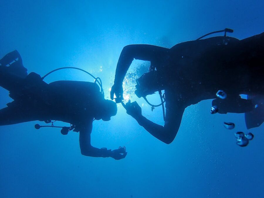 Two scuba divers sharing a moment underwater in bright blue ocean waters