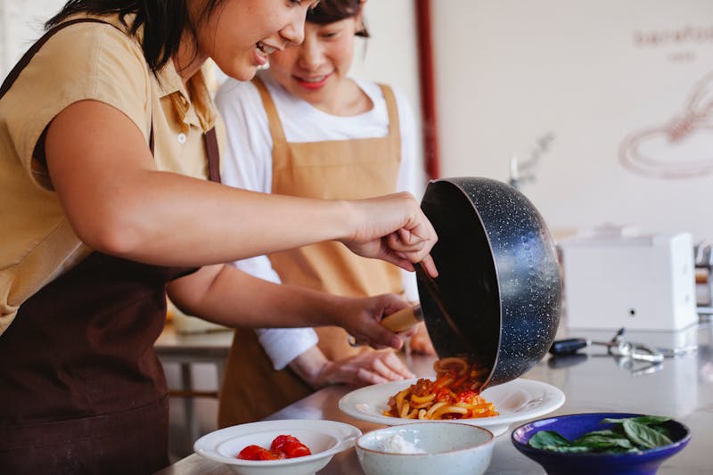 Two women preparing a pasta dish together in a cozy kitchen setting