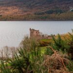 Urquhart Castle ruins overlooking Loch Ness surrounded by lush green hills in the Scottish Highlands