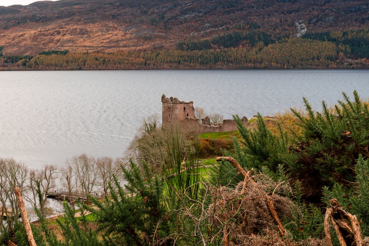 Urquhart Castle ruins overlooking Loch Ness surrounded by lush green hills in the Scottish Highlands