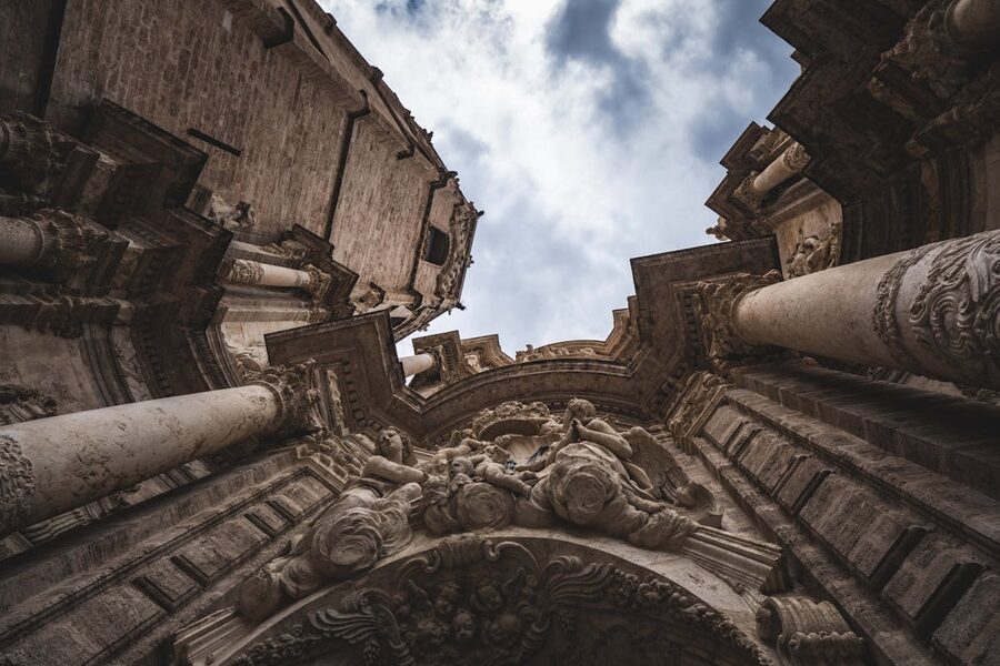 Dramatic upward view of an ornate Baroque cathedral facade with moody clouds in Valencia