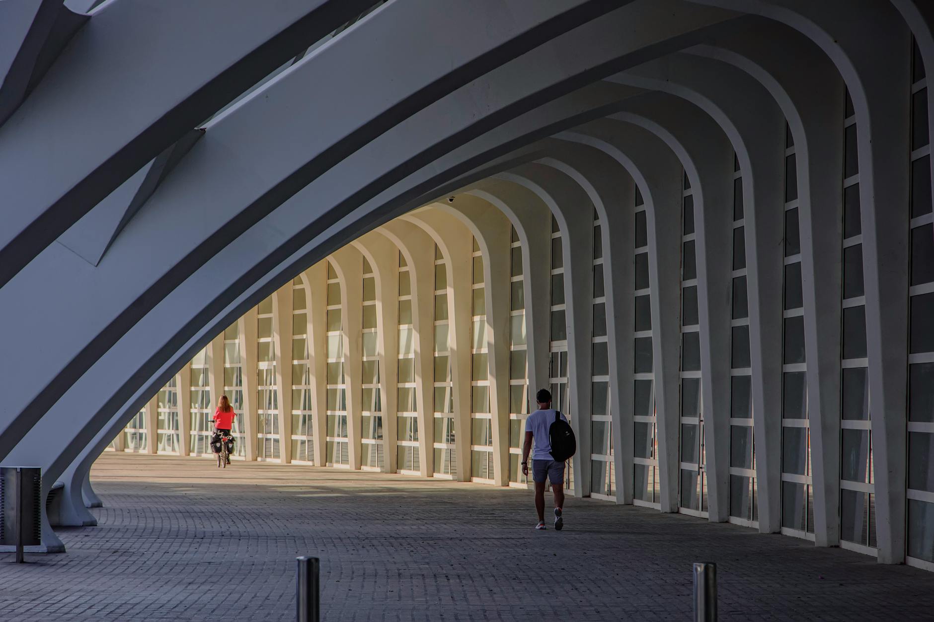Cyclist and pedestrian under modern arches in Valencia
