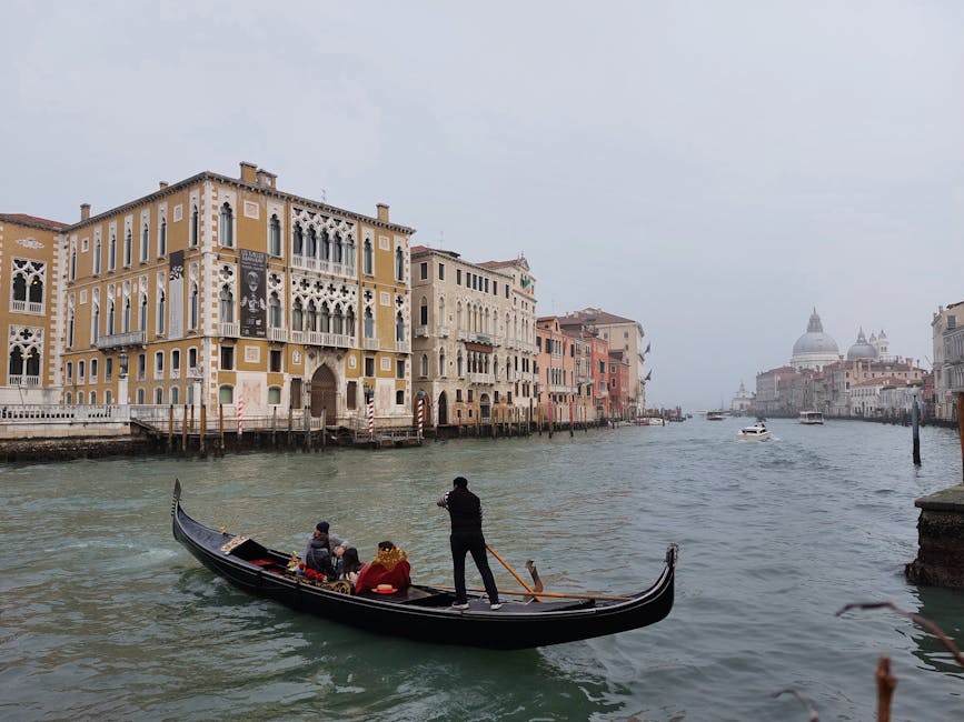 A gondolier rowing a gondola through a narrow Venice canal surrounded by colorful Venetian buildings