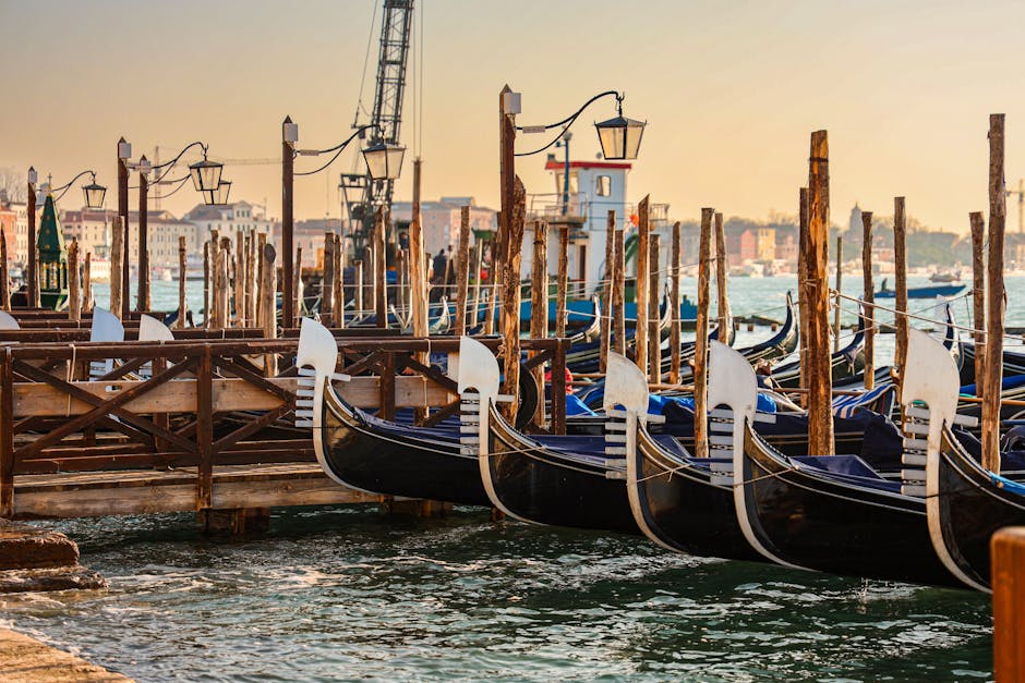 Several gondolas moored at their posts during sunrise in Venice with golden light on the water