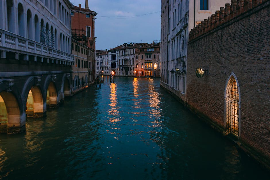 A serene Venice canal at twilight with warm lights from buildings reflecting on the calm water