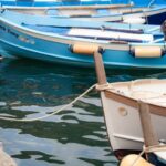 Colorful fishing boats moored in the small harbor of Vernazza, Cinque Terre, with pastel-colored buildings rising behind them