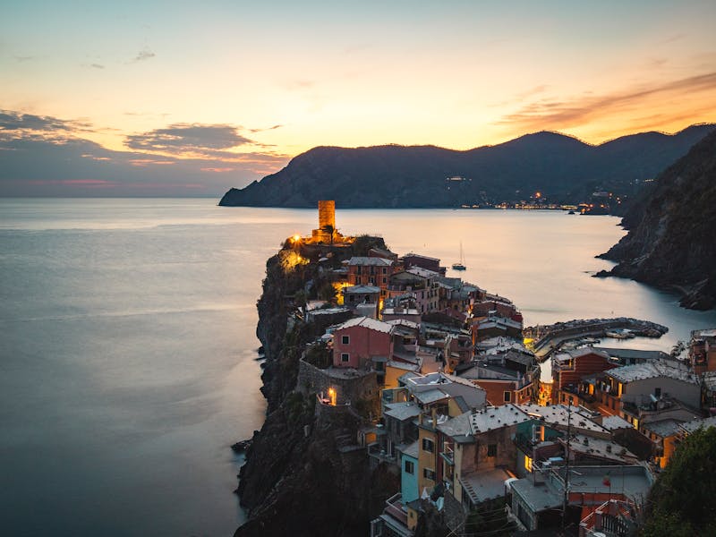 The village of Vernazza on the Cinque Terre coast glowing in warm orange sunset light against a dramatic sky