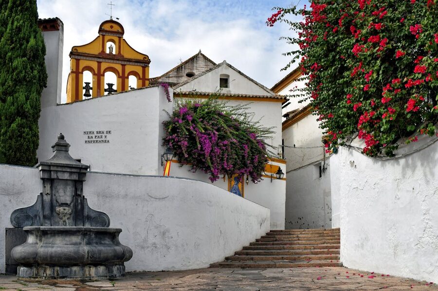 A picturesque alley in Cordoba featuring a church bell tower framed by bougainvillea