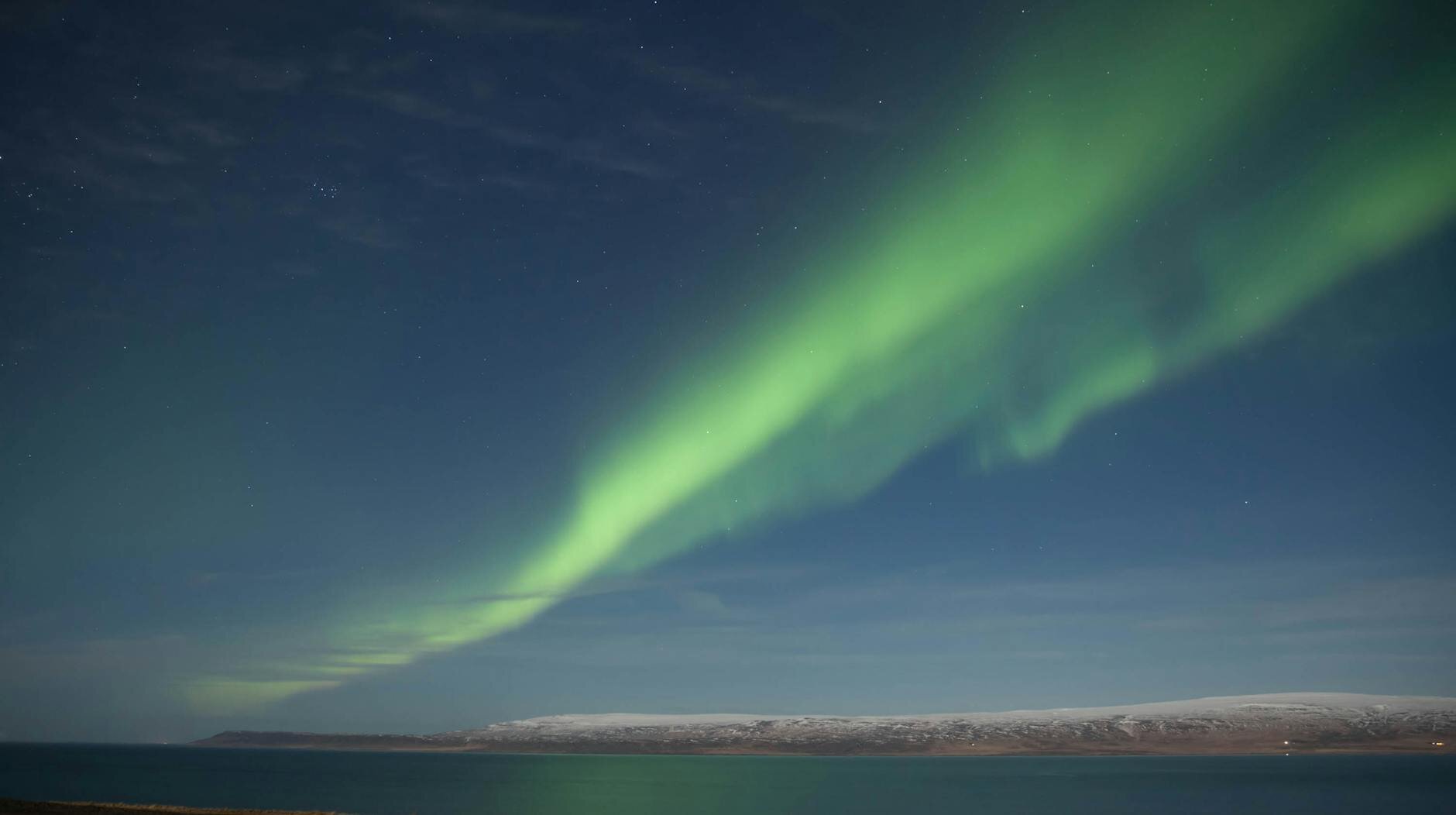 Radiant aurora borealis above sea and snow in BÃºÃ°ardalur, Iceland.