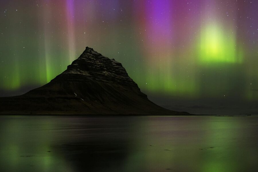Radiant northern lights dance over Iceland's unmistakable Kirkjufell mountain at night.