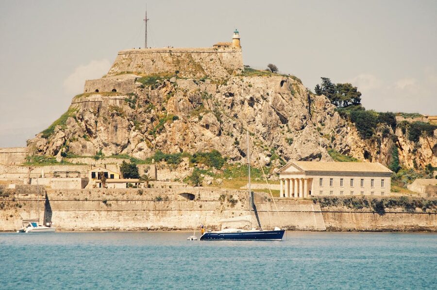 View of the historic Old Fortress in Corfu, Greece, with a sailing boat in the foreground.