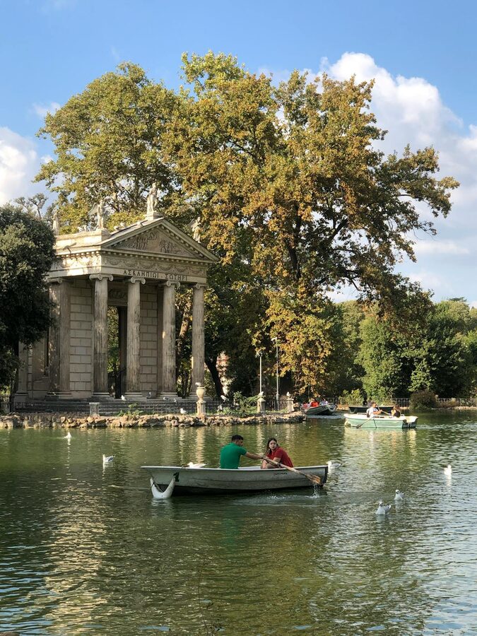 Boats on the lake at Villa Borghese with the Temple of Aesculapius visible through trees