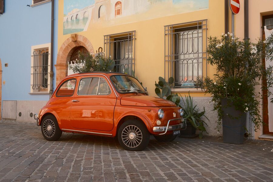 Classic orange Fiat car parked on a cobblestone street in Italy with colourful buildings