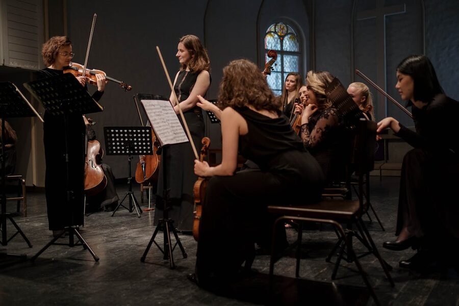 A group of female string musicians playing during an indoor rehearsal session