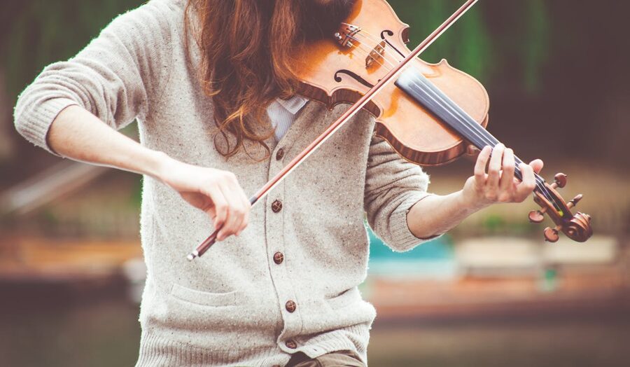 A violinist plays their instrument outdoors in warm golden light
