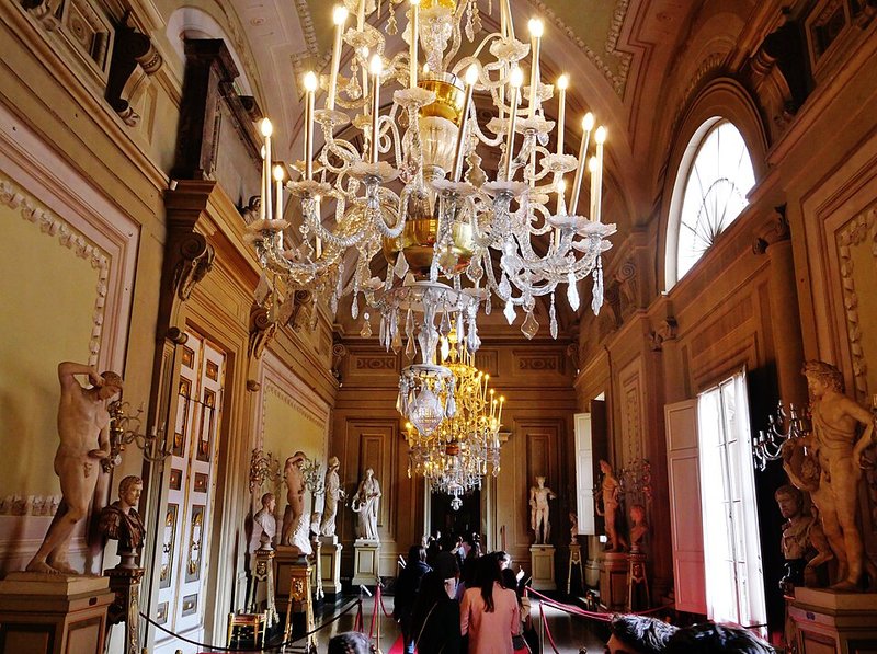 Ornately decorated room inside the Palatine Gallery at Palazzo Pitti with paintings covering the walls floor to ceiling