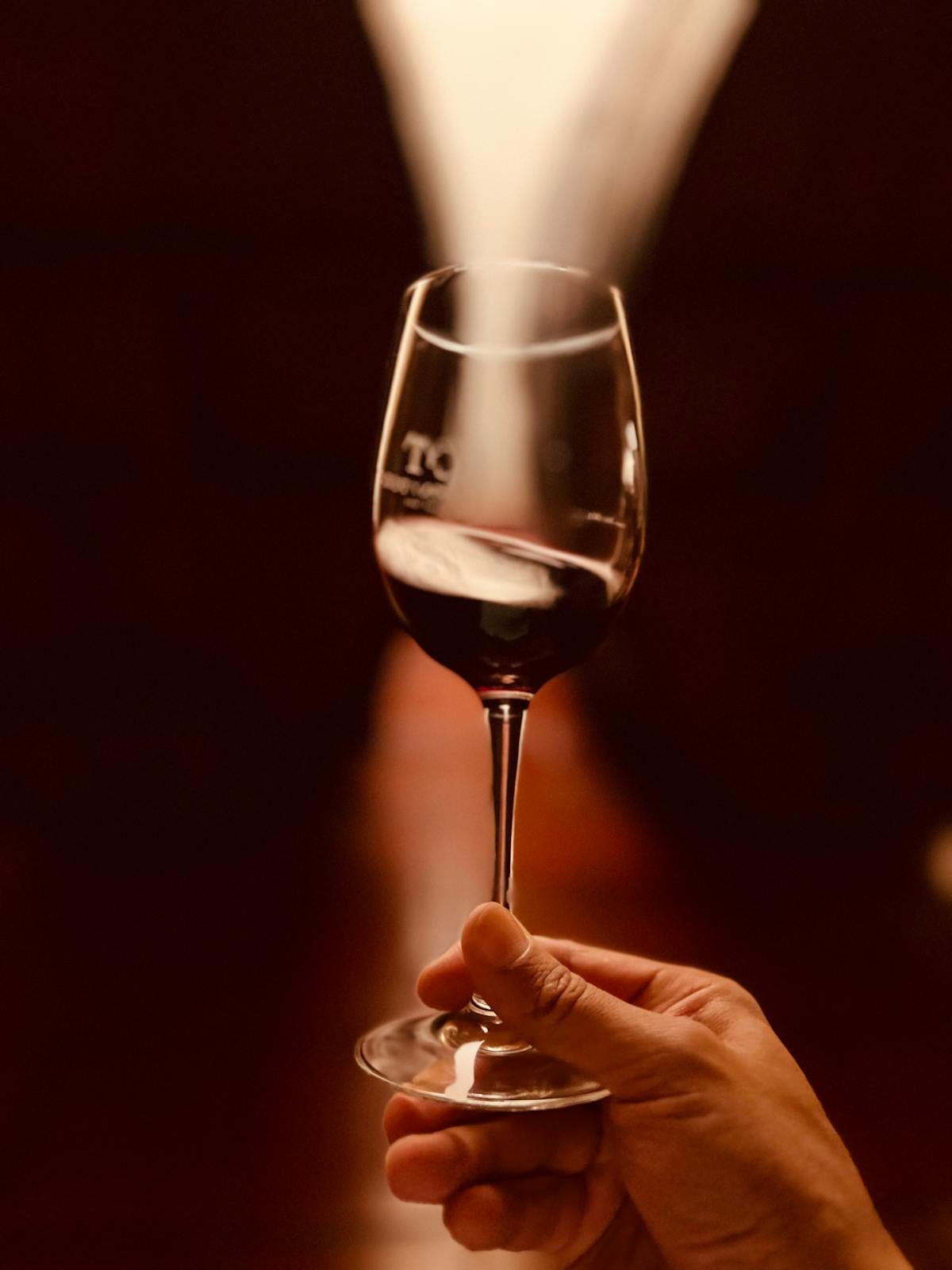 Hand holding a glass of red wine with warm blurred background