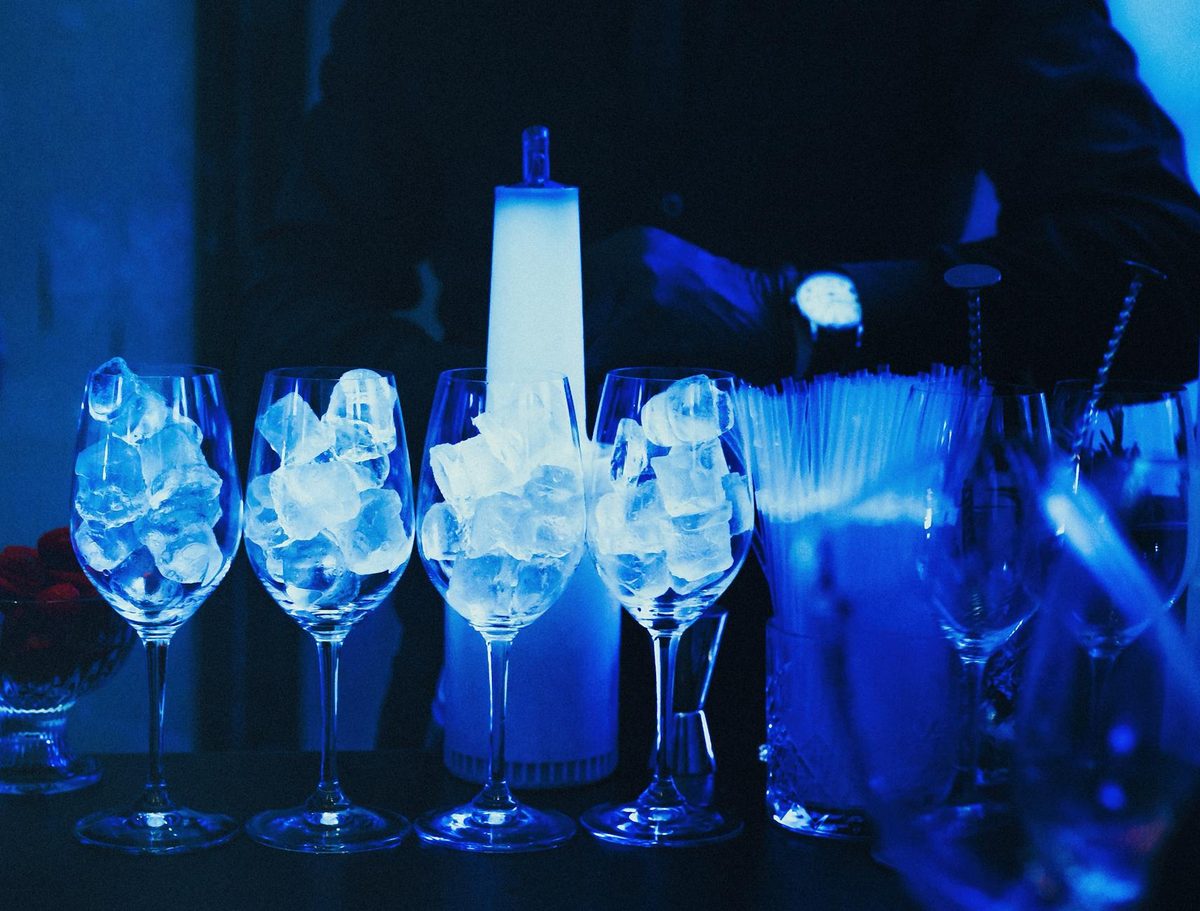 Wine glasses filled with ice at a bar under blue lighting