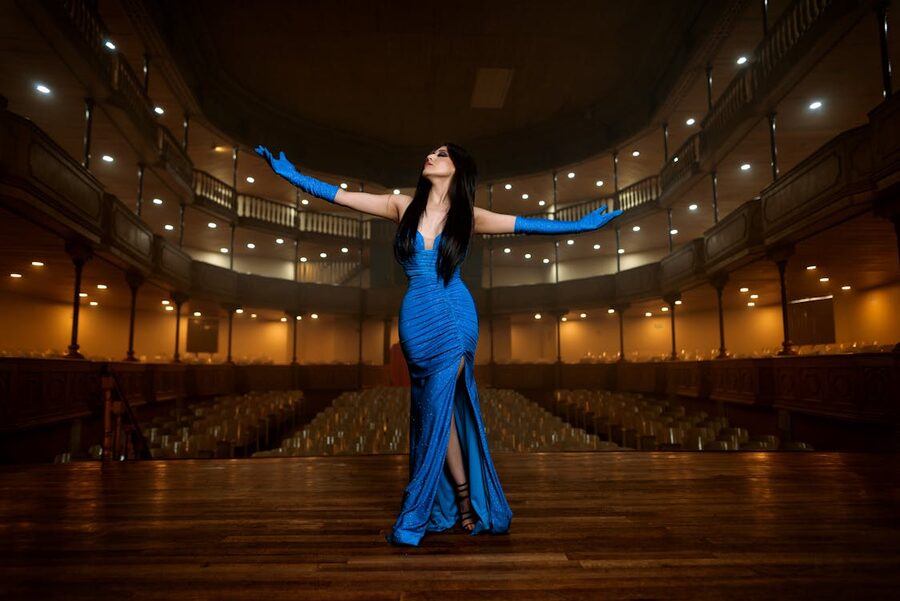 A woman in a blue dress performing on a grand theater stage with dramatic lighting