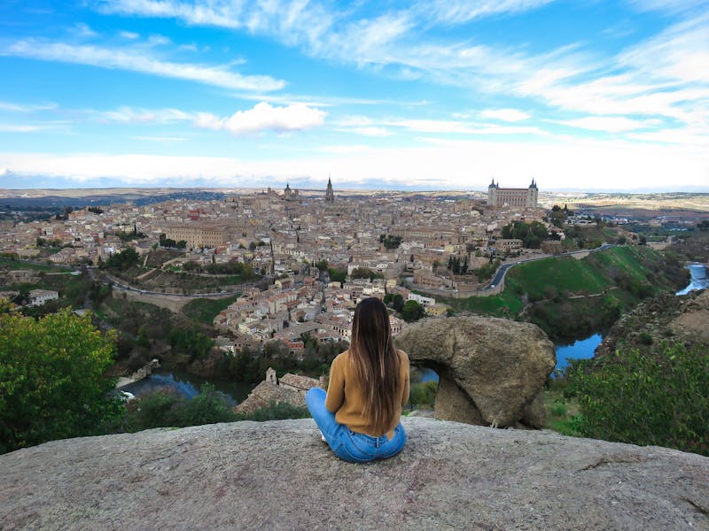 Woman sitting on a cliff edge overlooking the panoramic view of Toledo Spain