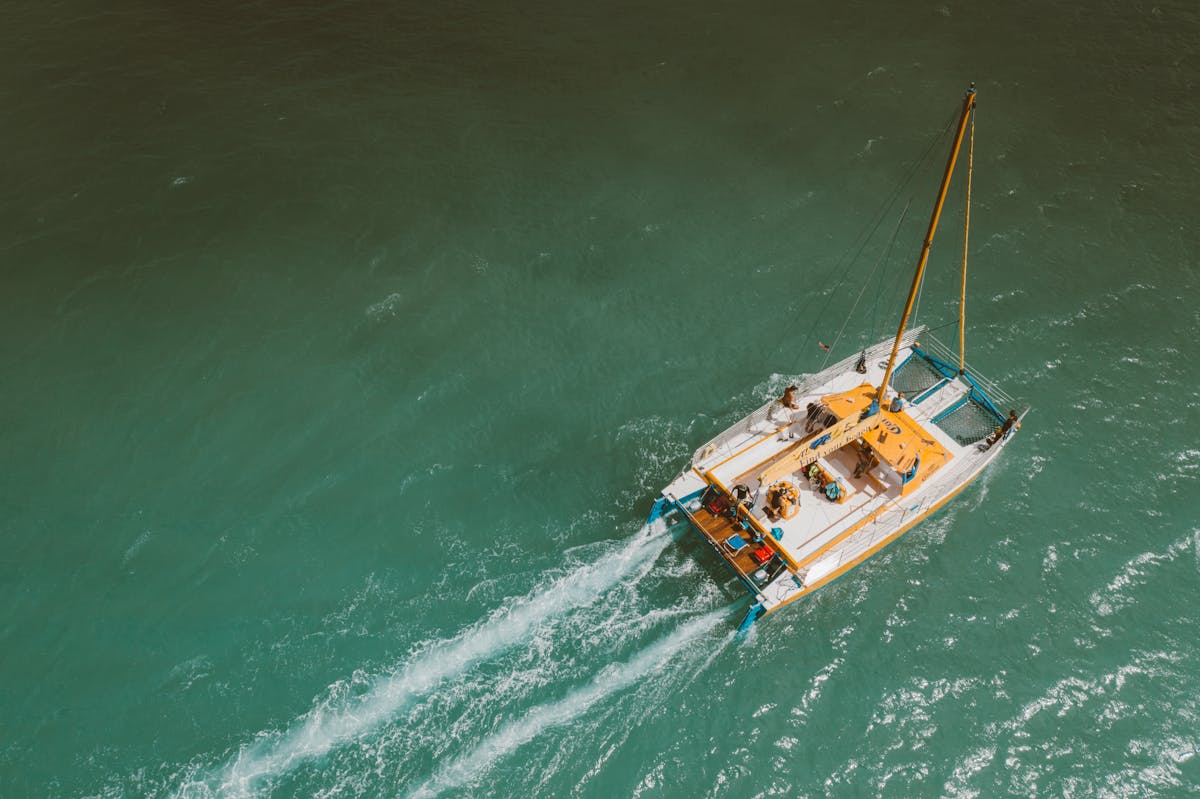 Aerial view of yacht sailing in clear turquoise water with swimmers