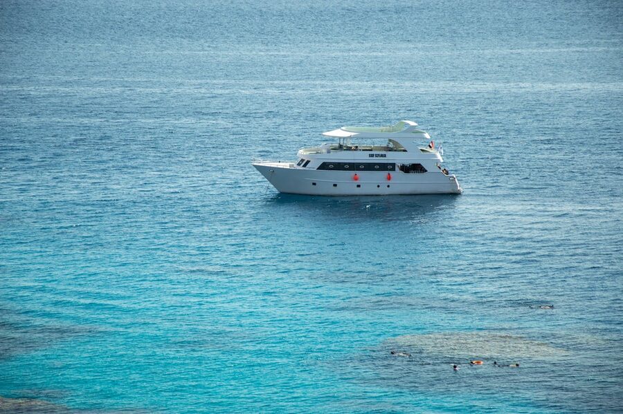 Luxury white yacht on clear blue sea with snorkelers swimming nearby