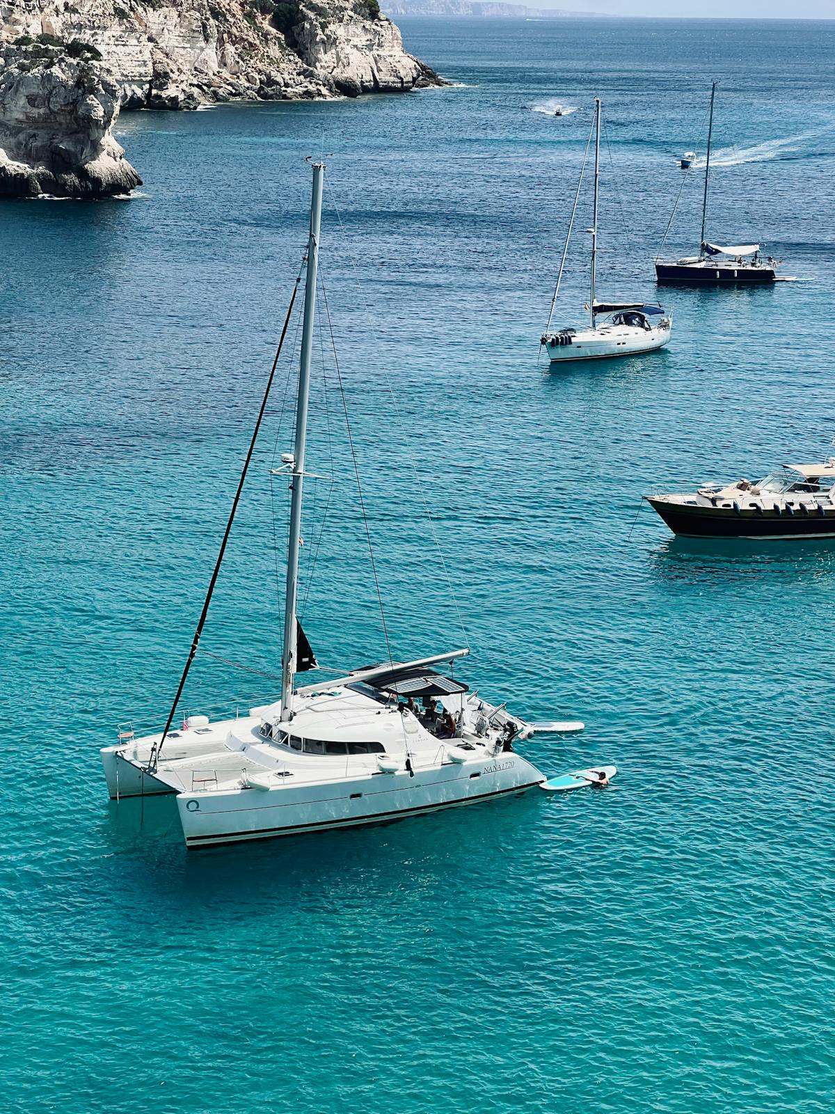 Yacht sailing in crystal clear turquoise waters near rocky cliffs
